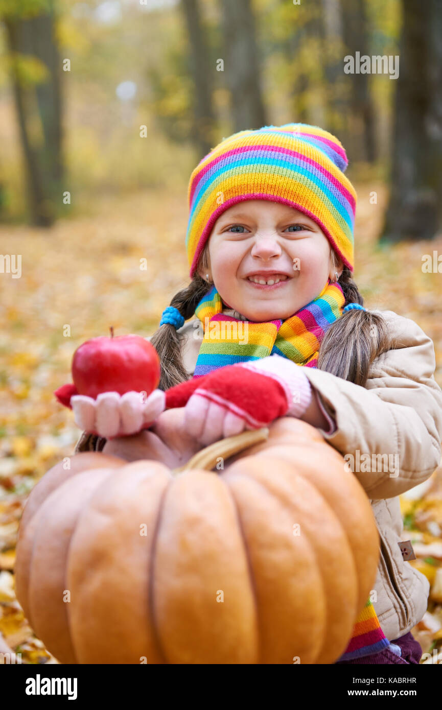 child eat apple and pumpkin in forest, sit on autumn leaves background ...