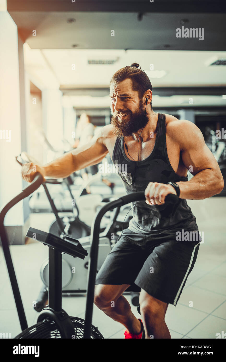 young man using exercise bike at the gym. Fitness male using air bike ...
