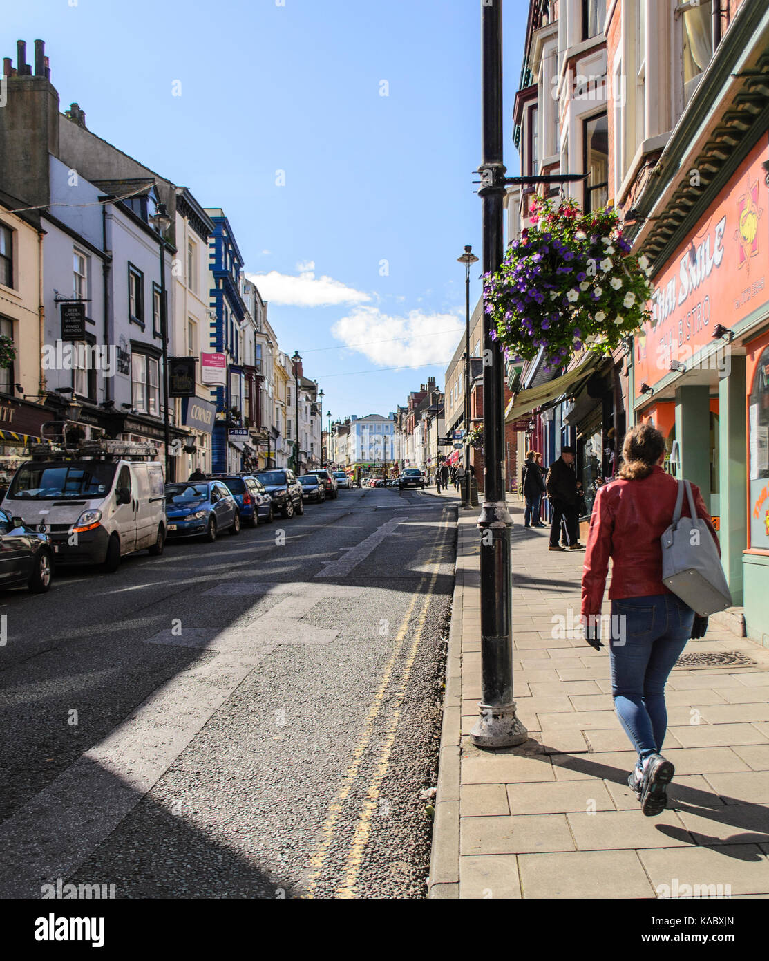 A street scene with a woman in red jacket walking along pavement away ...