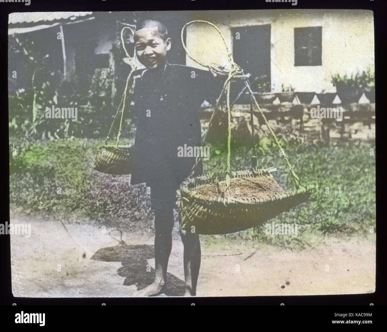 Smiling boy holding two baskets on a shoulder pole, China, ca. 1918 ...