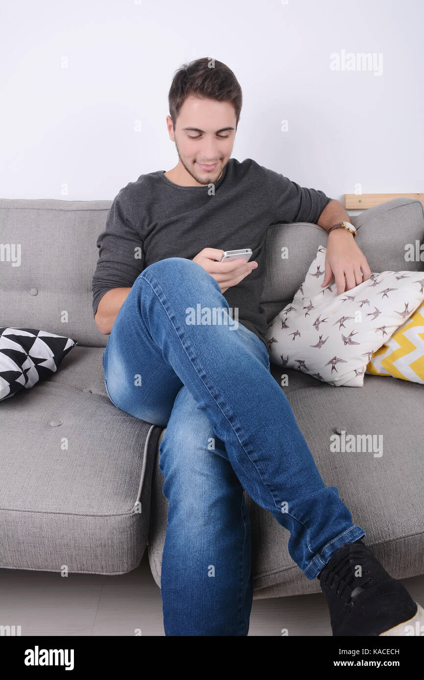 Attractive young man using his smartphone and relaxed on couch. Indoors ...