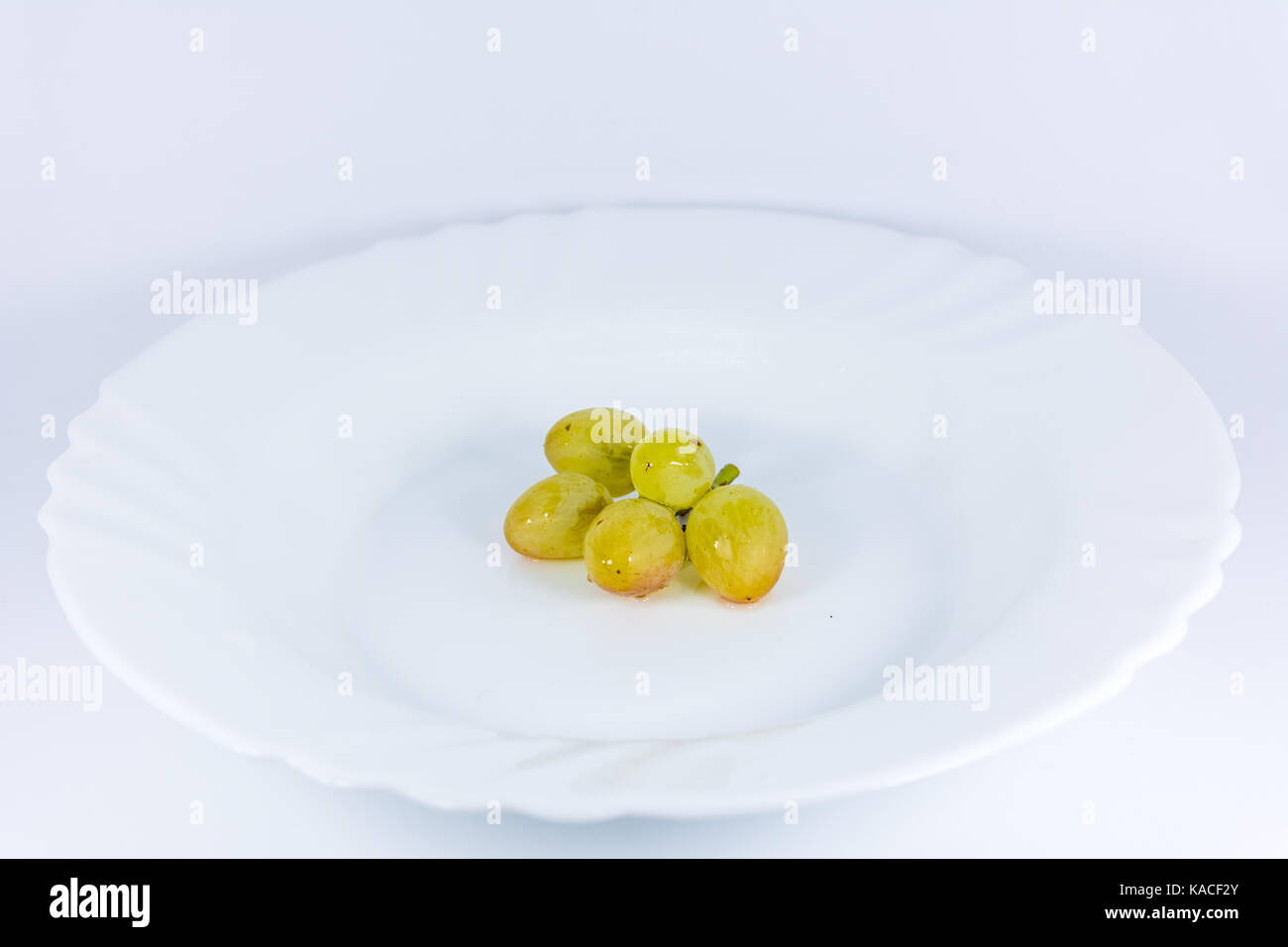 Little white grapes on white plate isolated Stock Photo - Alamy