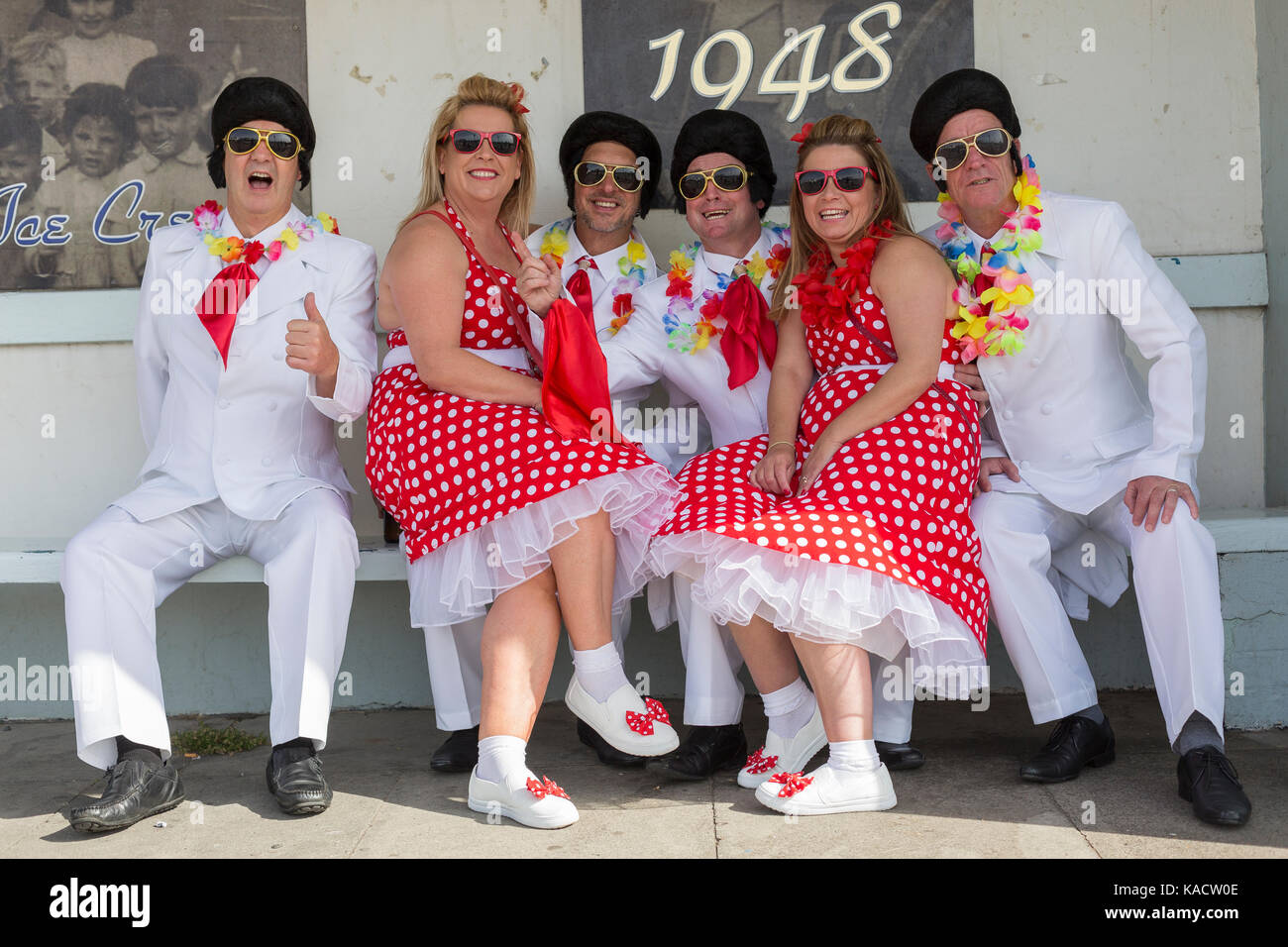 Elvis fans in red and white costumes sat on bench with 1948 poster ...