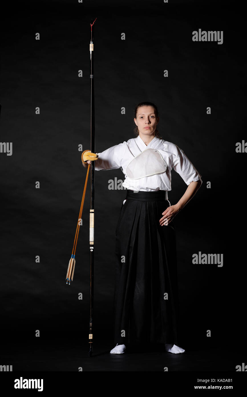 Caucasian woman practicing traditional Kyudo Japanese archery on black ...