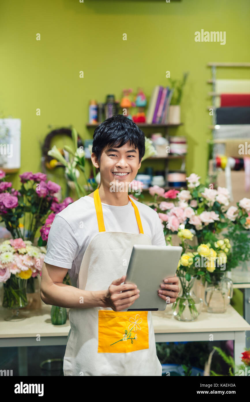 Happy asian male florist using digital tablet at counter in flower shop ...