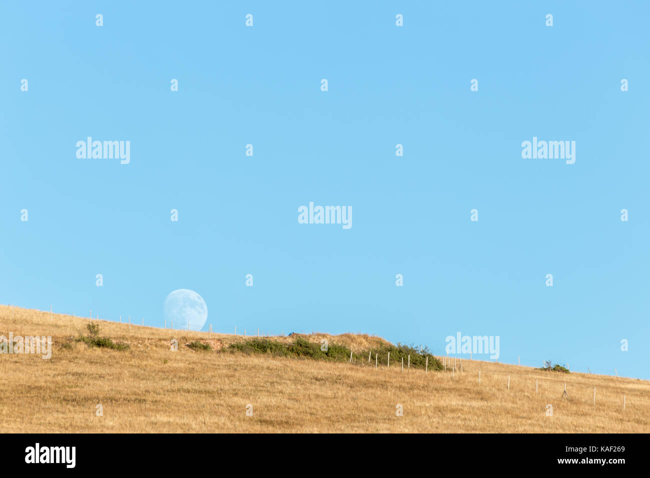 Moon rising up behind an hill, with an empty, blue sky Stock Photo - Alamy