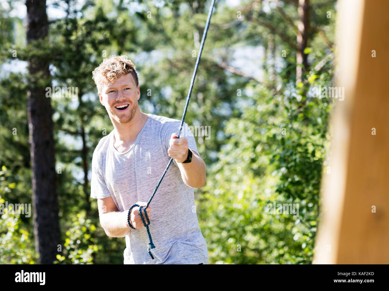 Man Smiling While Pulling Rope Attached To Wooden Structure Stock Photo ...