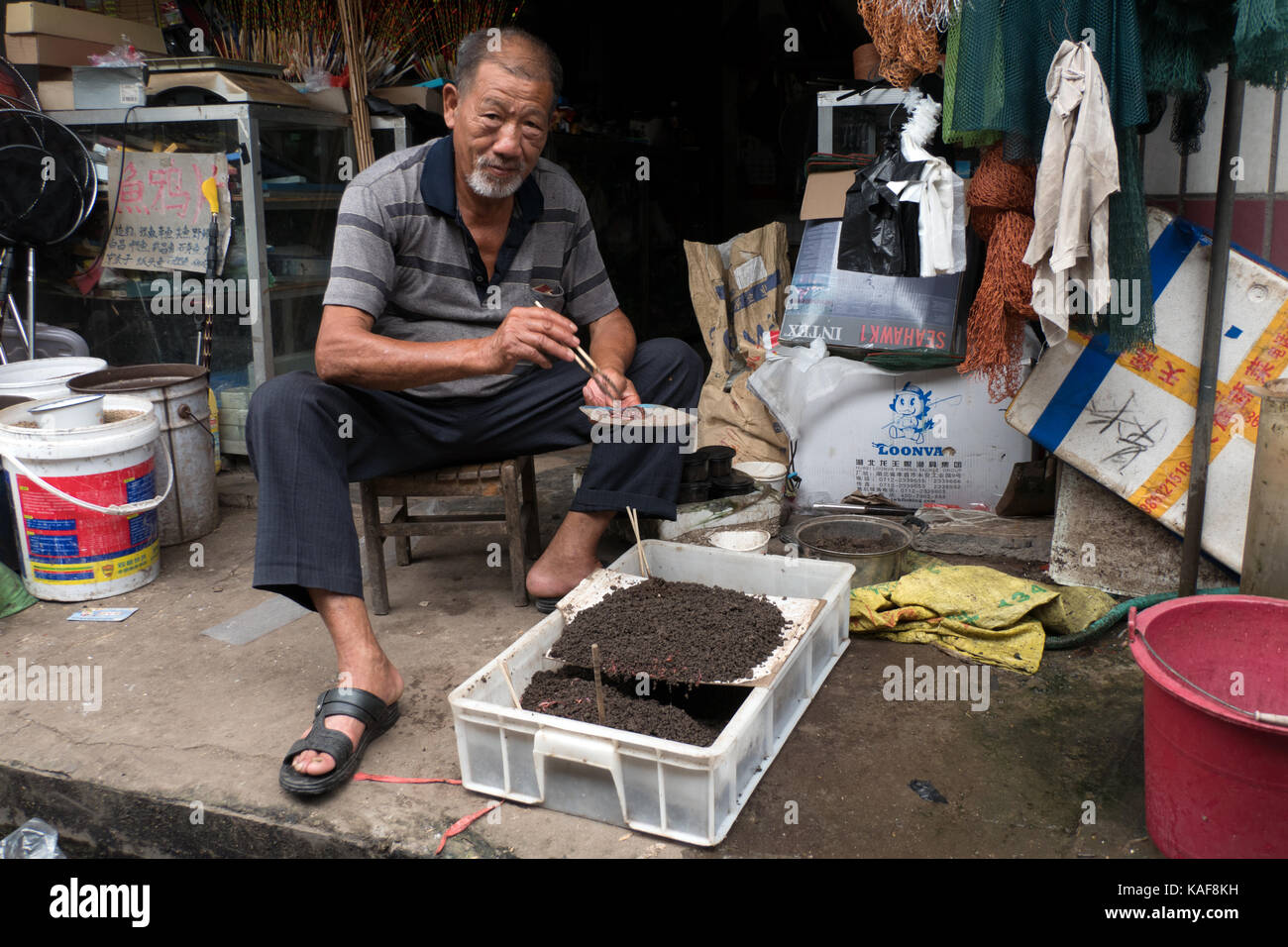 Portrait of a Chinese man in a shop selling worms as fishing bait in a ...