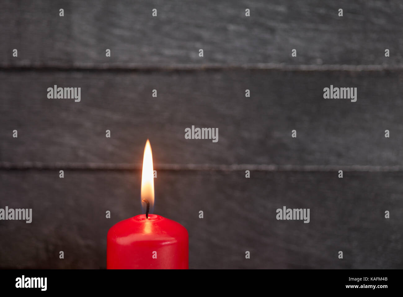 Burning red candle with flame makes candlelight on wooden background ...