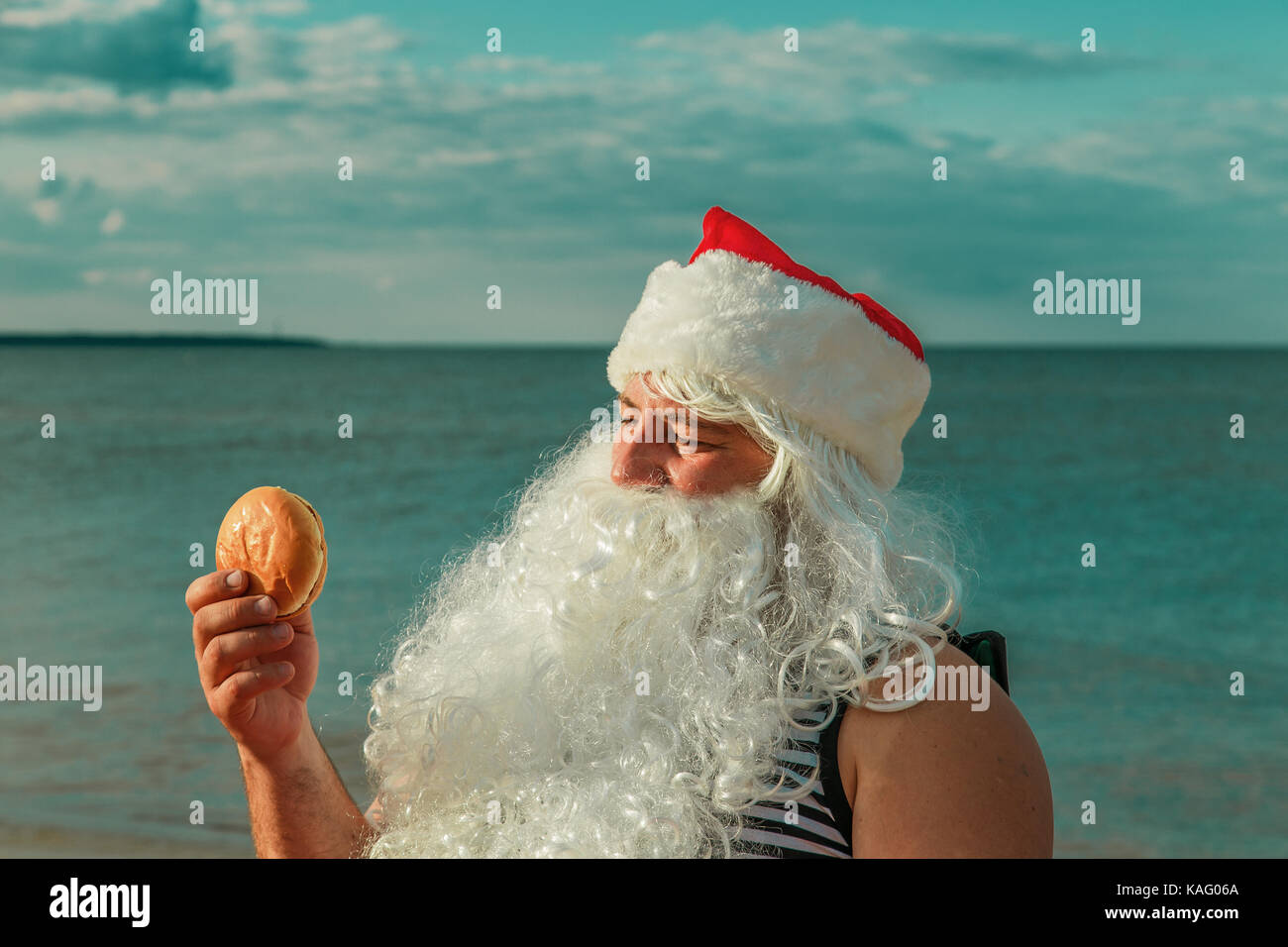 Santa Claus on the beach eating a hamburger. The concept of unhealthy ...
