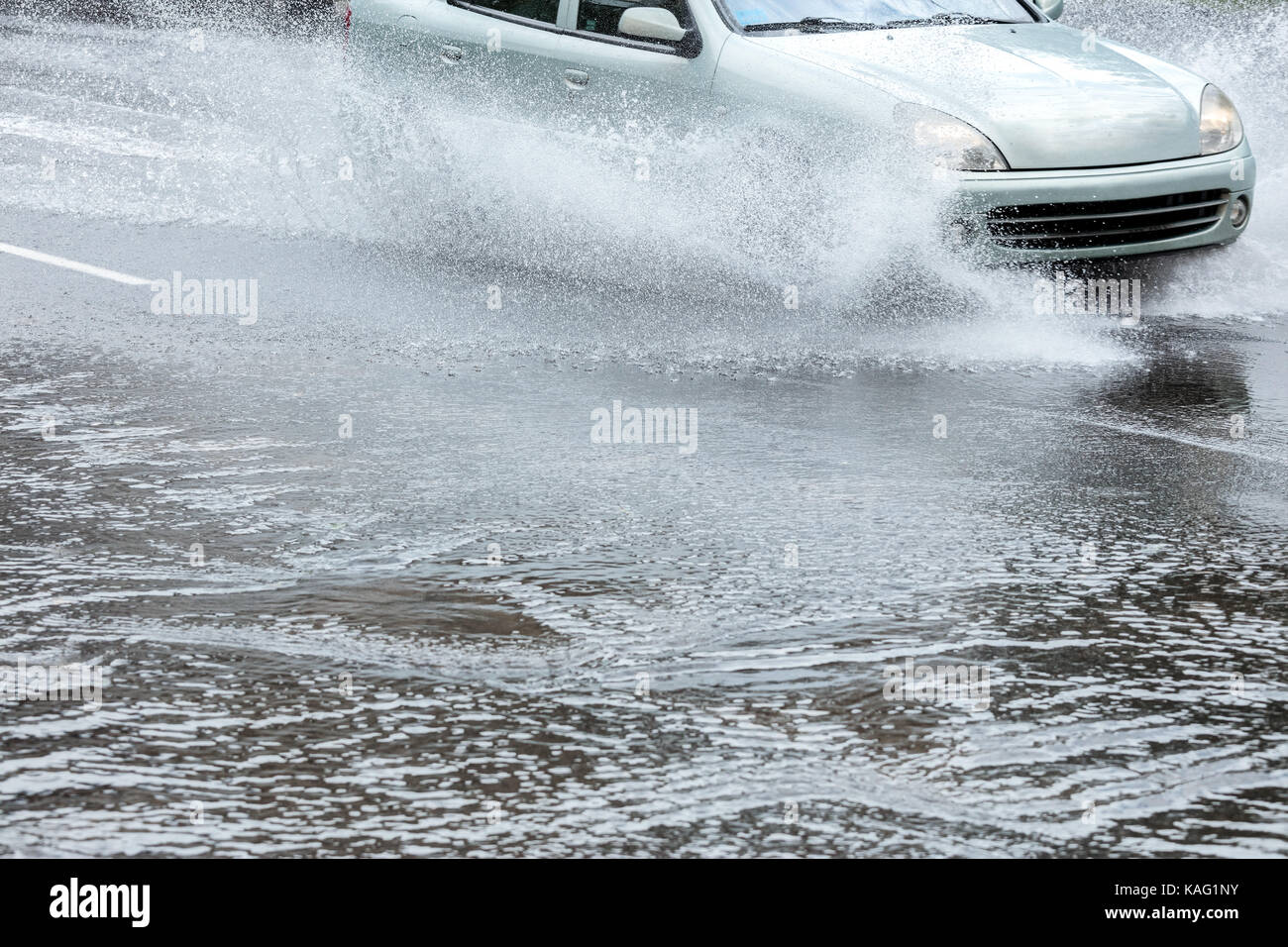 car driving on flooded city road through puddles creating water ...
