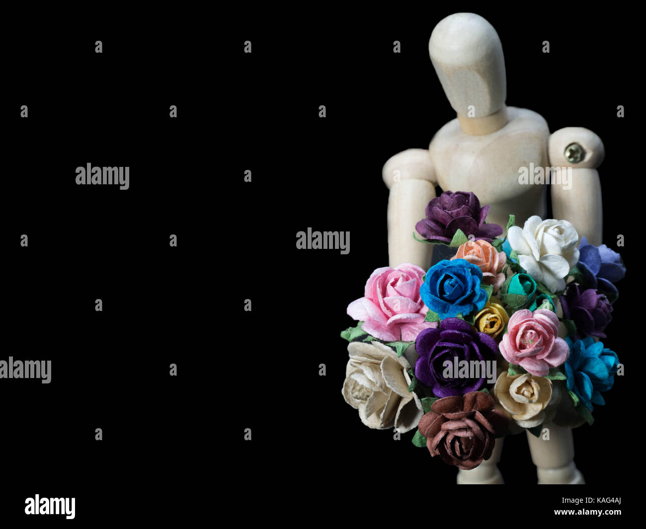 A wooden puppet holds a flower on a black background Stock Photo - Alamy