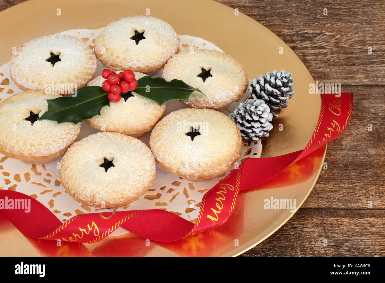 Christmas mince pies with holly and red ribbon on a gold plate on oak ...