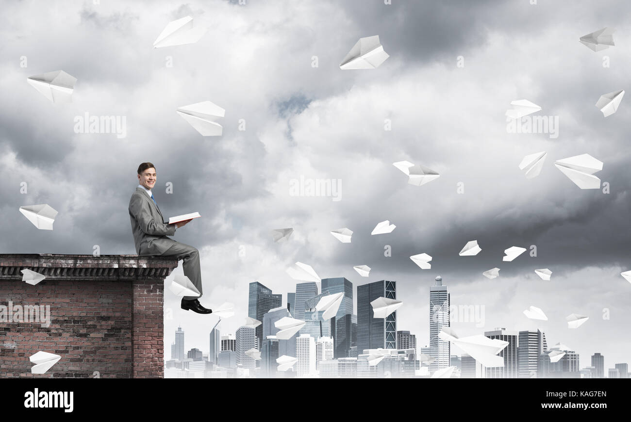 Man on roof edge reading book and cityscape at background Stock Photo ...