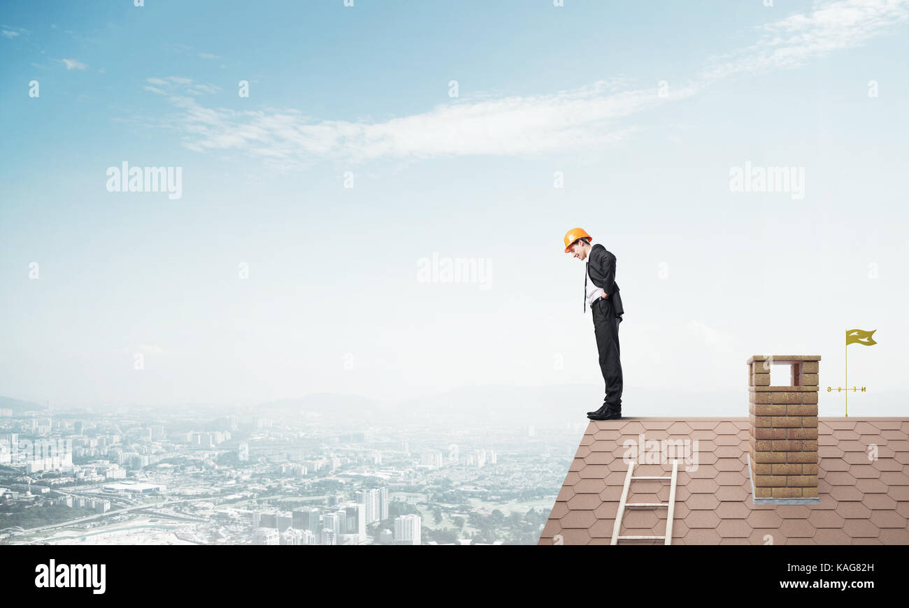 Businessman looking down from roof and modern cityscape at background ...