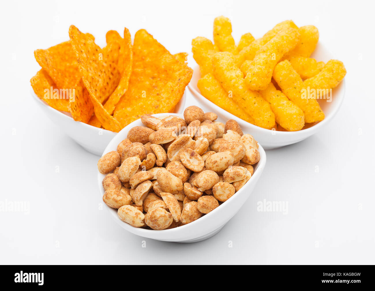 Cheese corn snacks and nachos with salty peanuts in white bowl on white ...