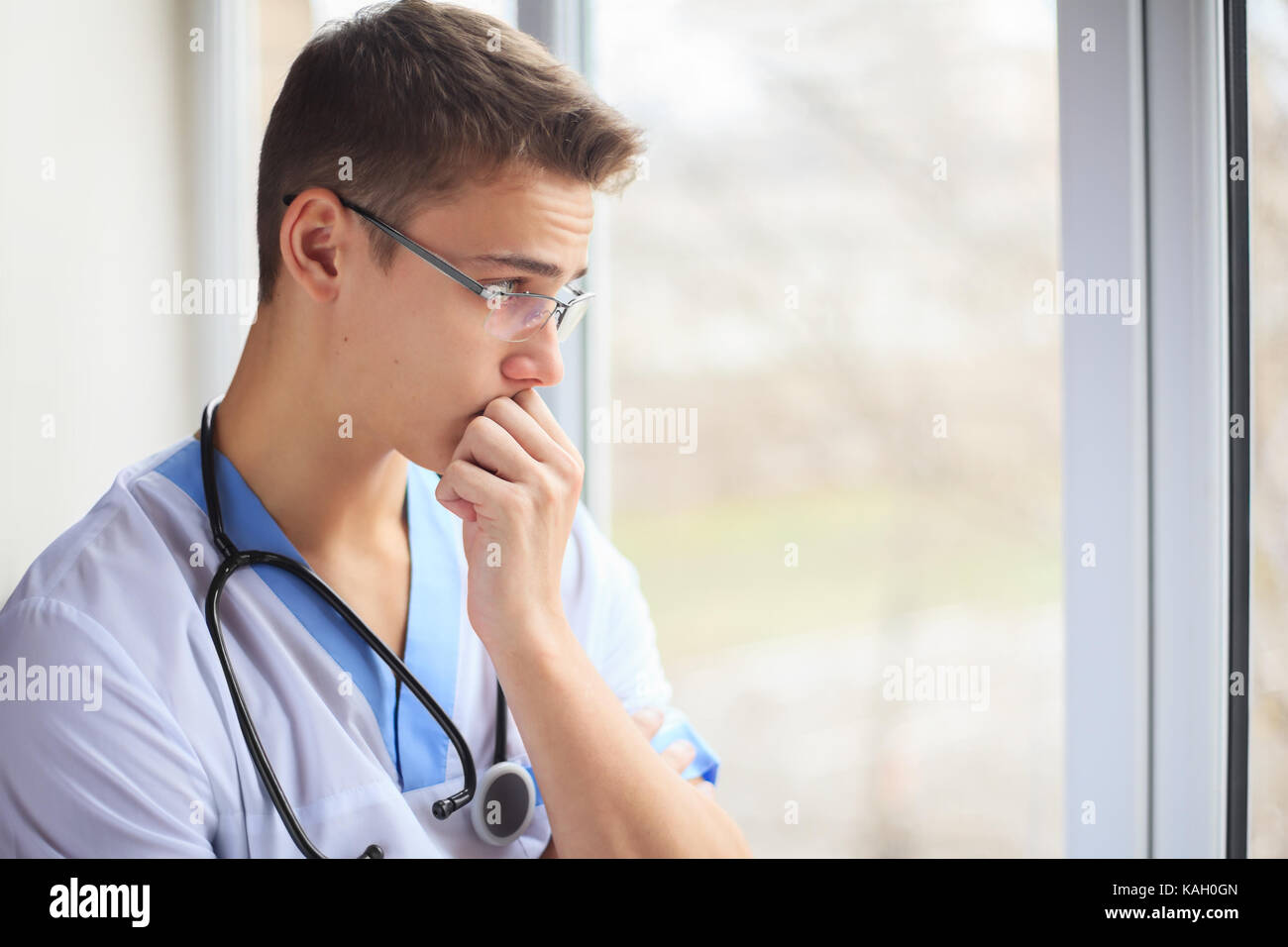 Portrait of thoughtful young doctor thinking with hand on his chin near ...