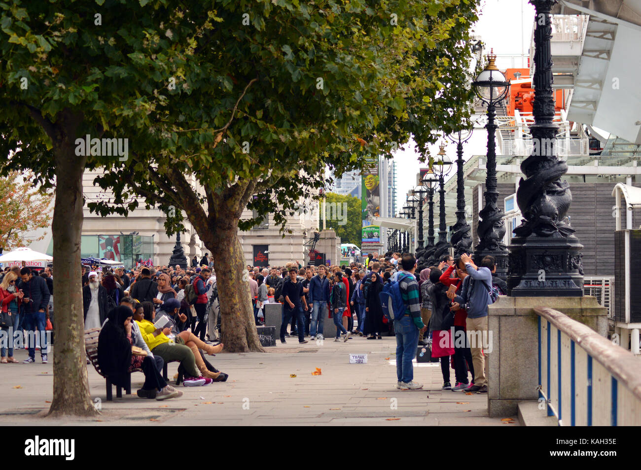Crowds queuing and milling around the London Eye, some people looking ...