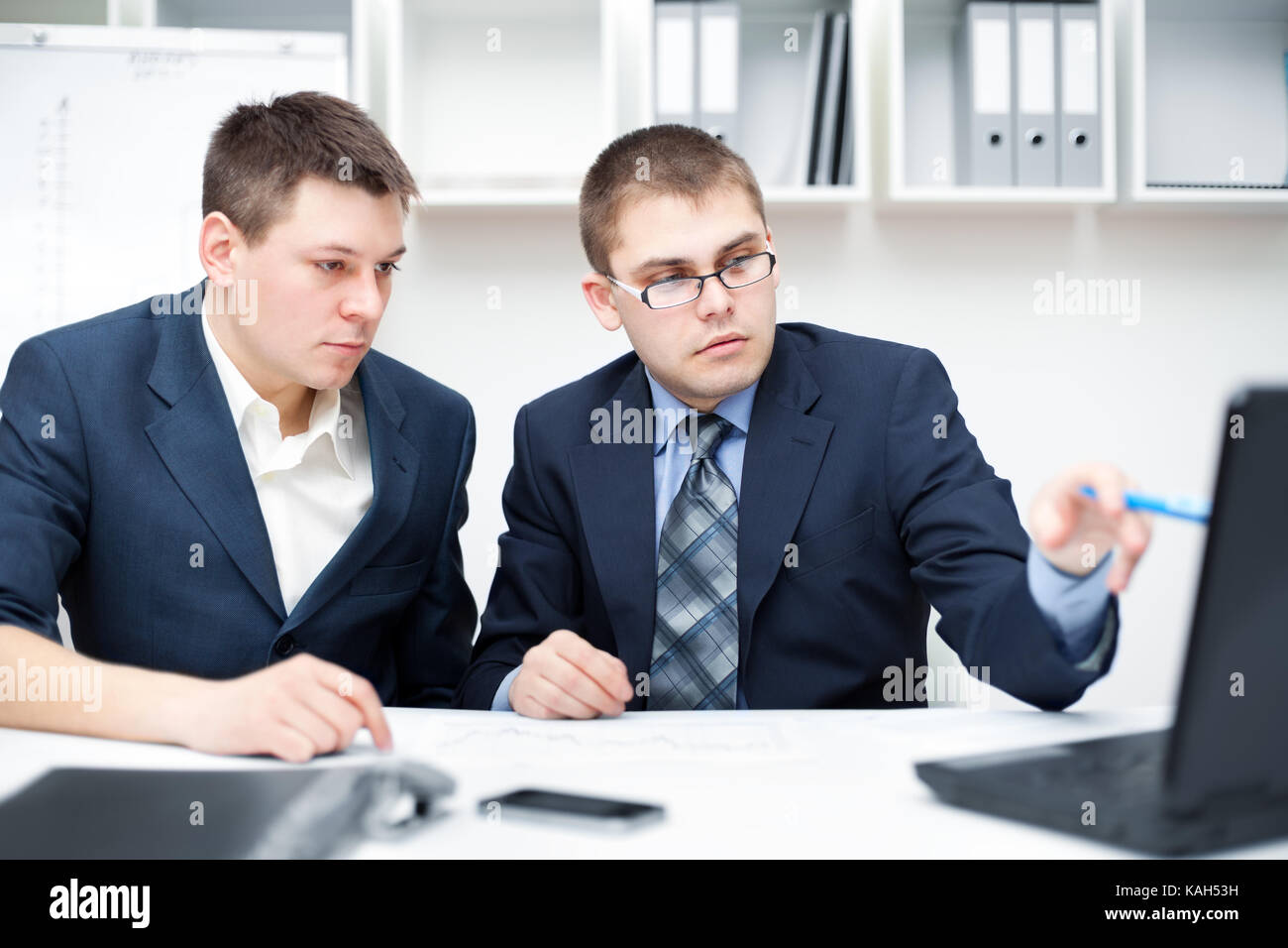 Two young businessmen working together with computer at office desk ...