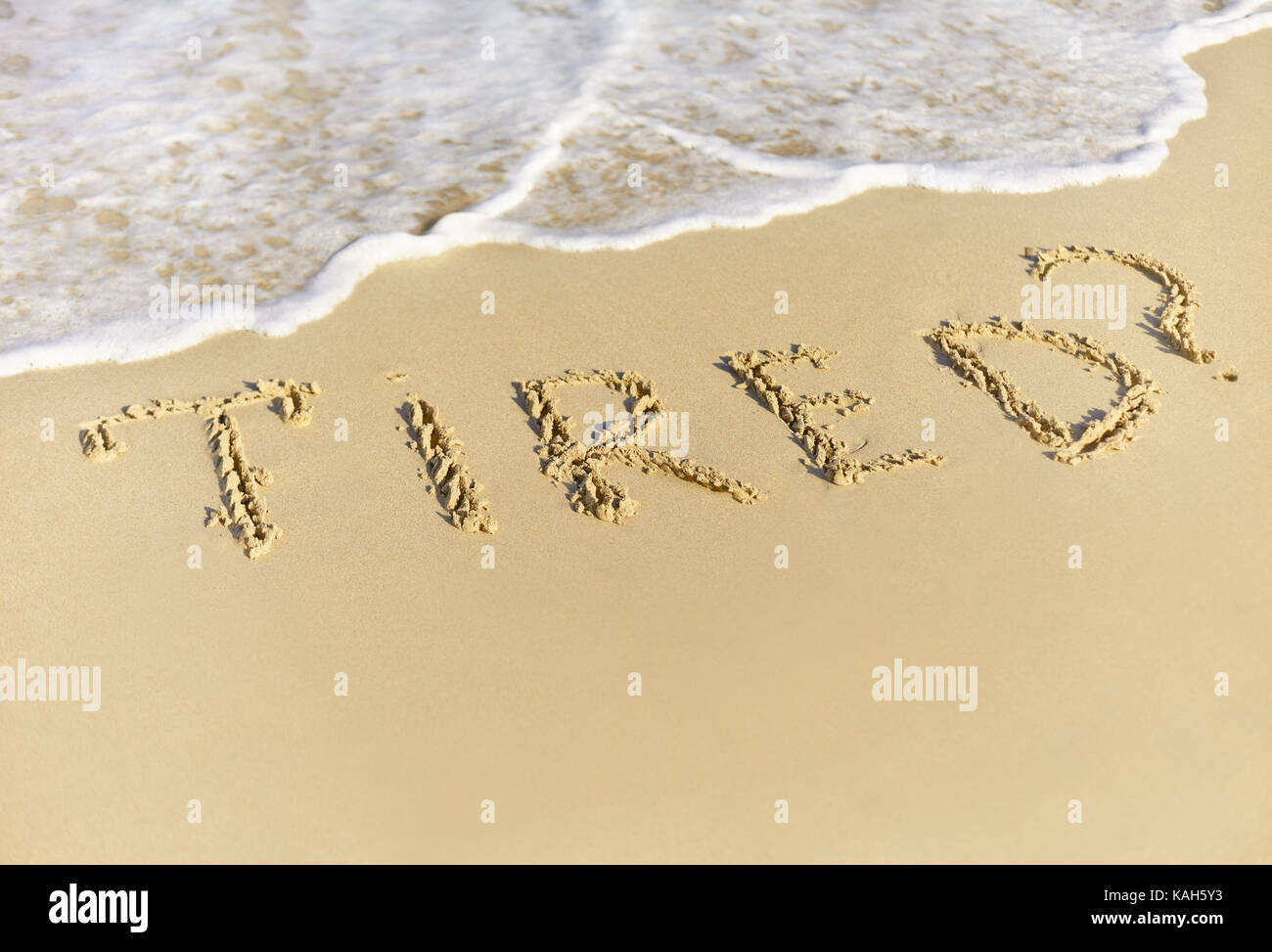 Tired - written by hand in sand on a sea beach, with a soft wave ...