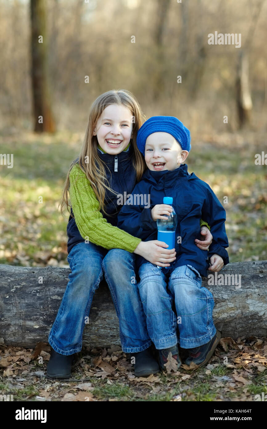 Two happy kids together with water bottle sitting on a big log in ...