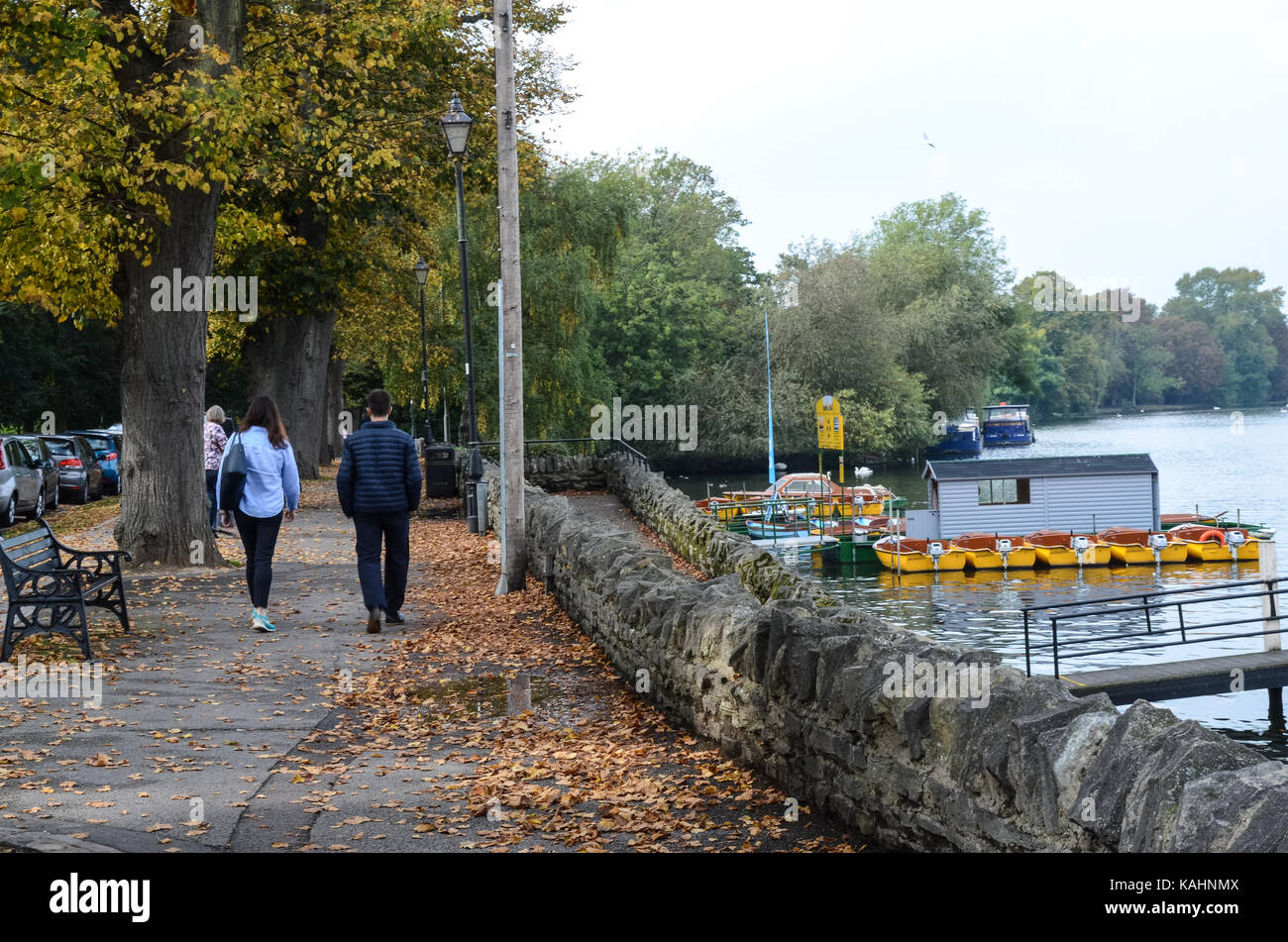 A couple walk along a leaf covered footpath alongside The River Thames ...