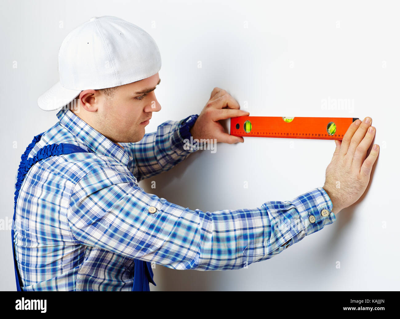 Young construction worker using spirit level on white wall Stock Photo ...