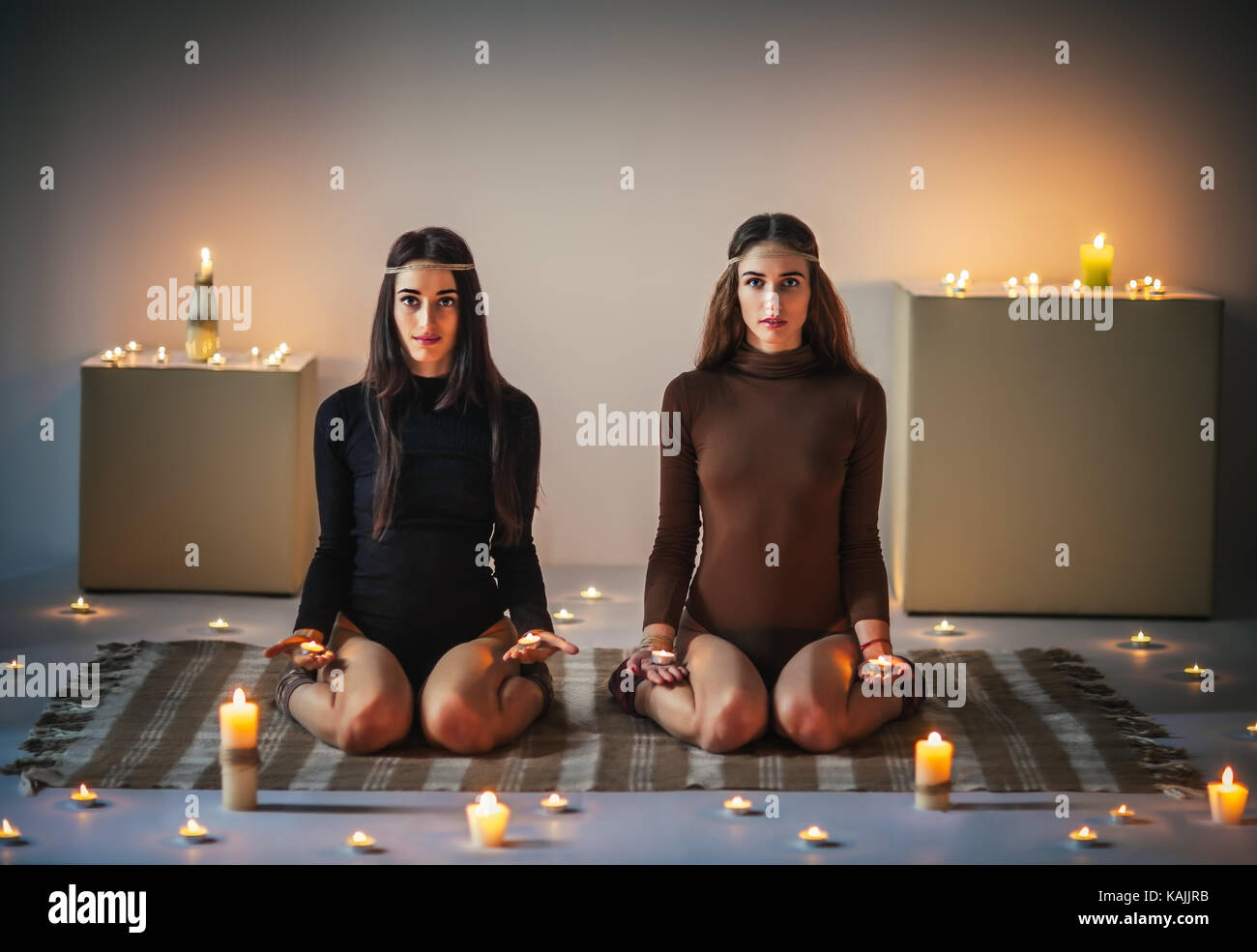 Two young women doing yoga asana diamond pose with candles in hands on ...