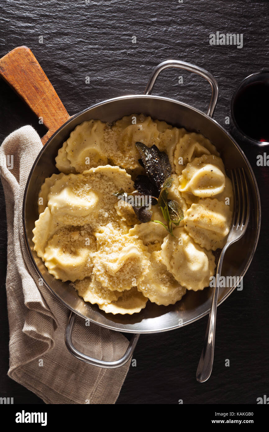 cooked ravioli in serving pan with parmesan and fried sage . on black ...