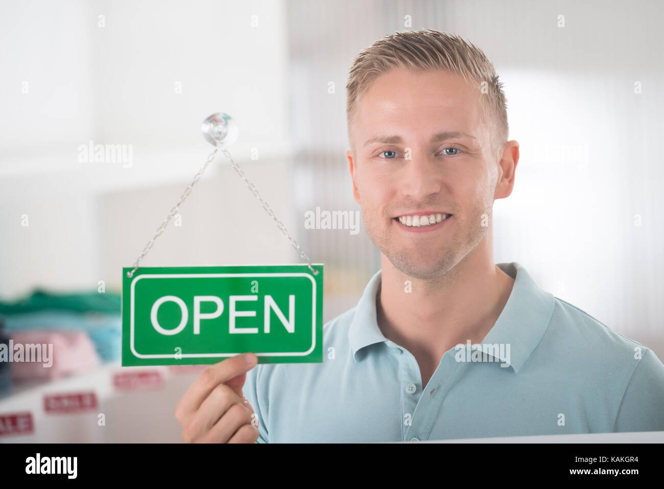 Portrait of confident male owner holding open sign in clothing store ...