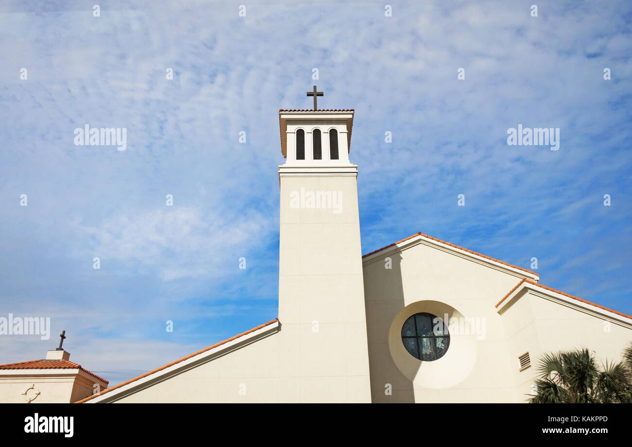 A tan stucco church with a tower and cross on top with a palm tree and ...