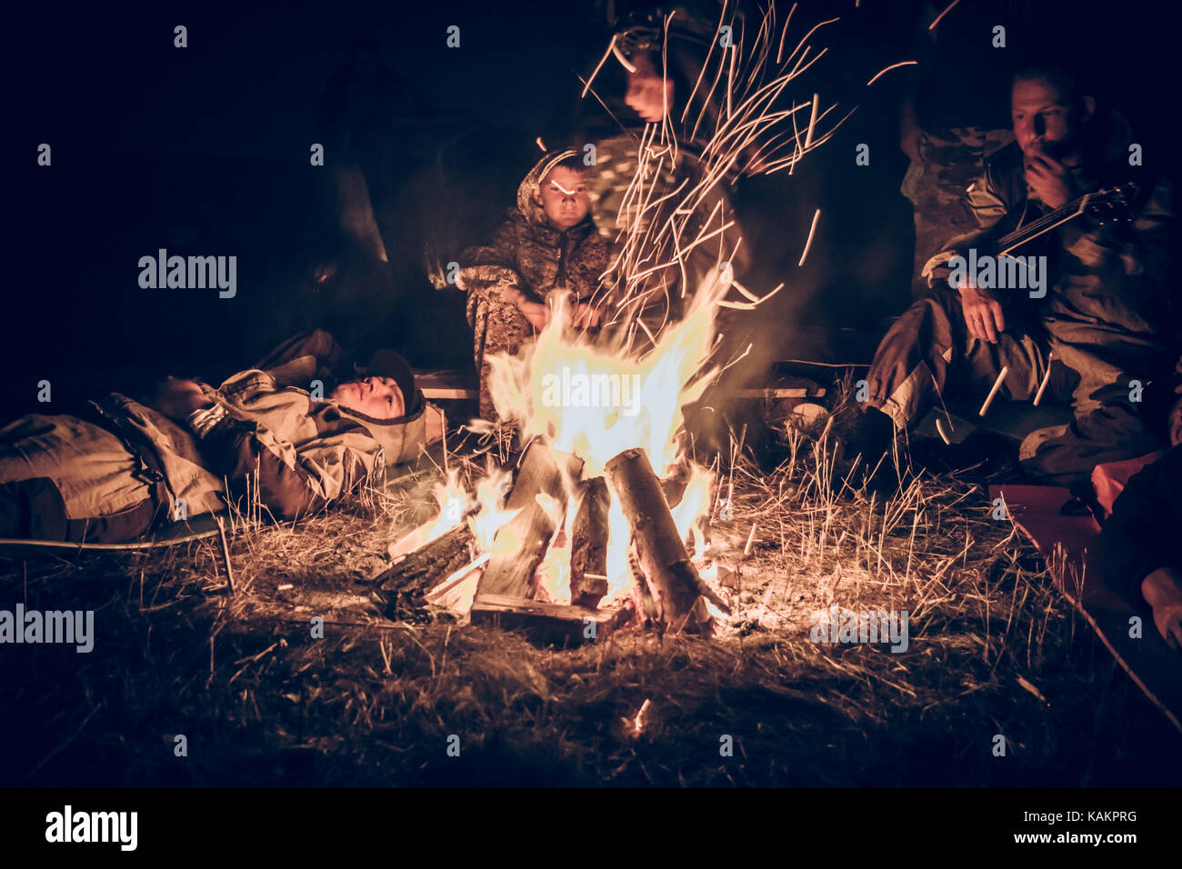 Group of people tourists relaxing by the fire in outdoors camp after ...