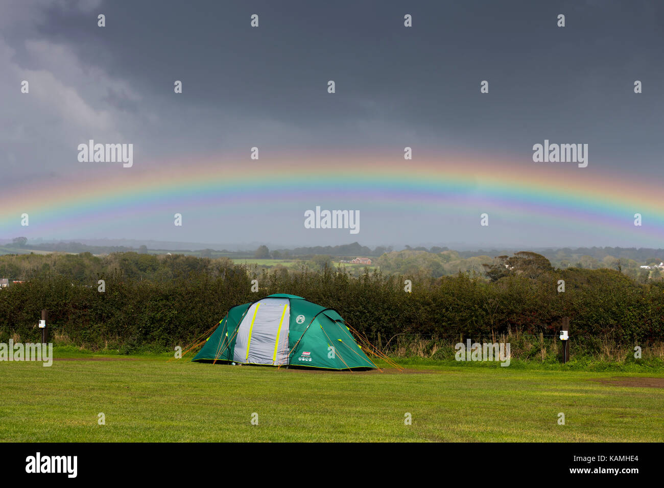 A tent in a green field with a rainbow overhead with a dark sky Stock ...