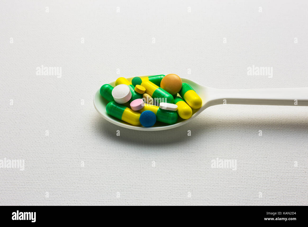 Many tablets and capsules pills on a spoon on white canvas background ...