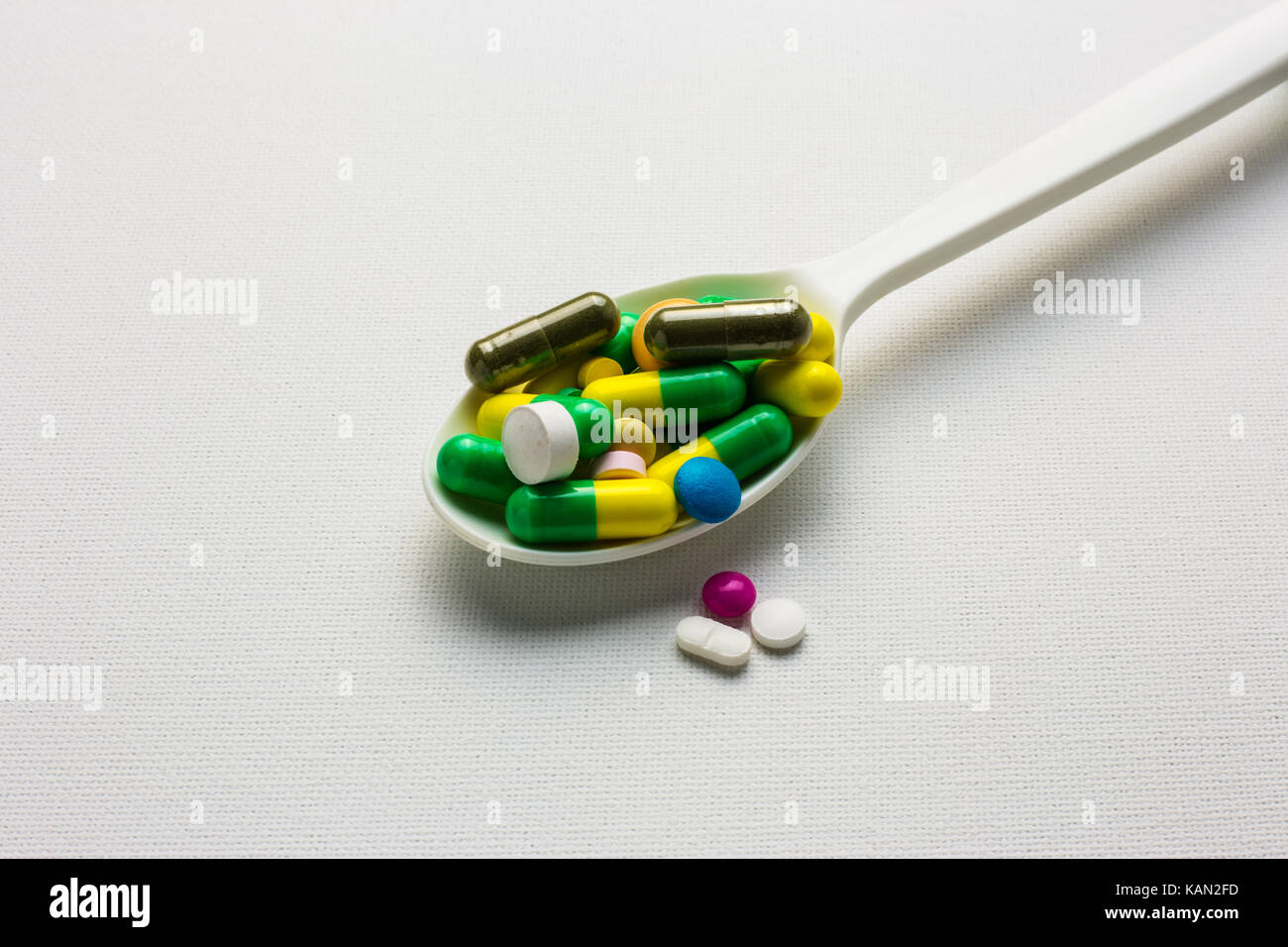 Many tablets and capsules pills on a spoon on white canvas background ...