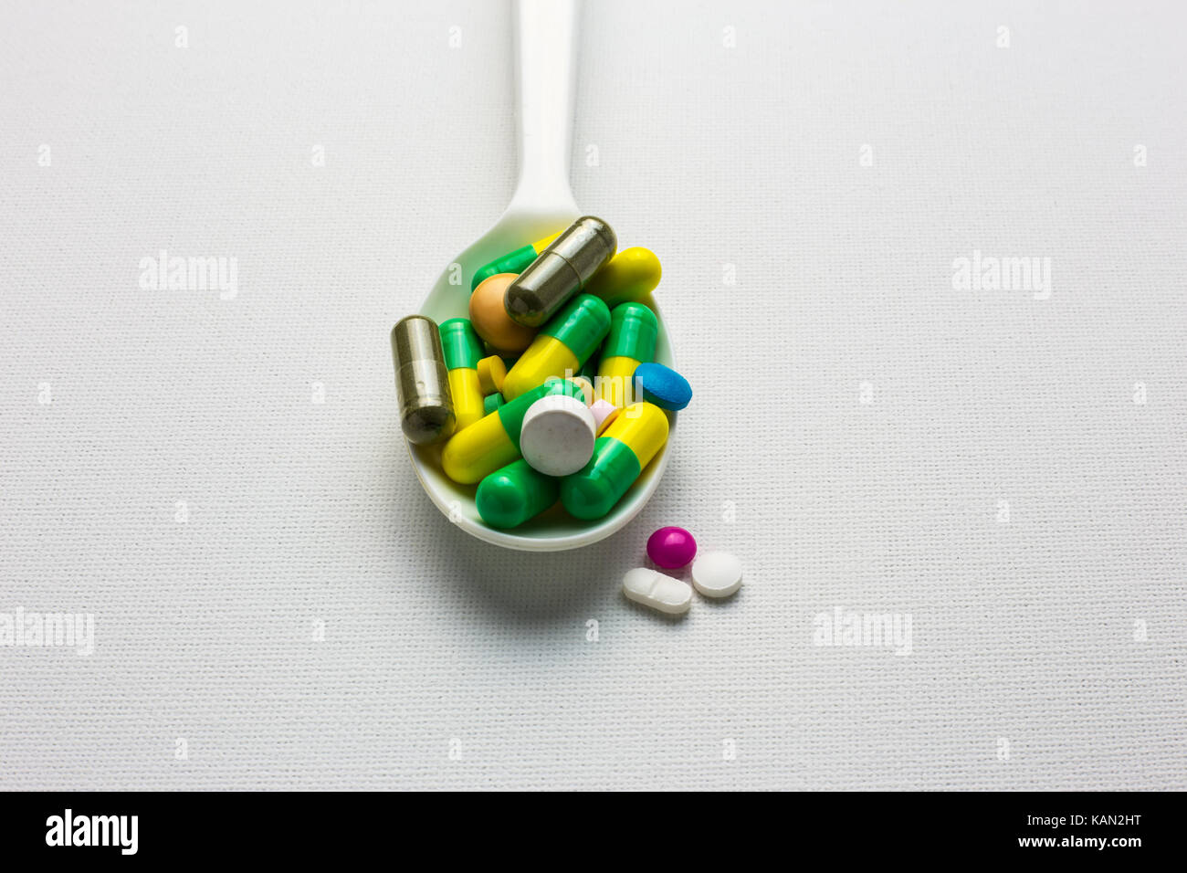 Many tablets and capsules pills on a spoon on white canvas background ...