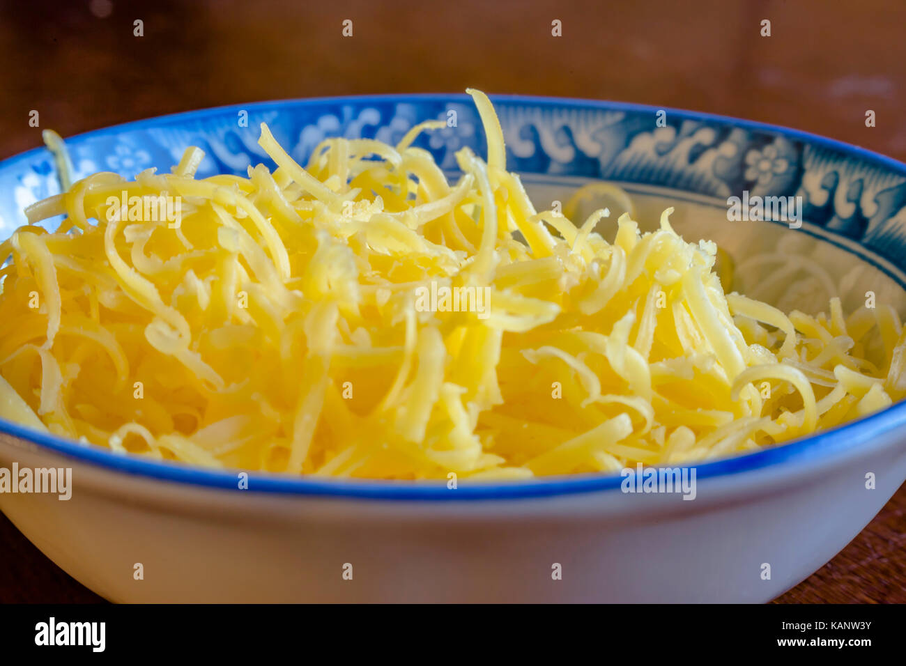 Grated mozzarella and cheddar cheese in dish over wooden background ...