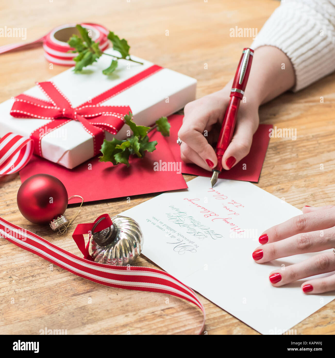 young woman writing christmas cards with red nails, a red pen, and ...