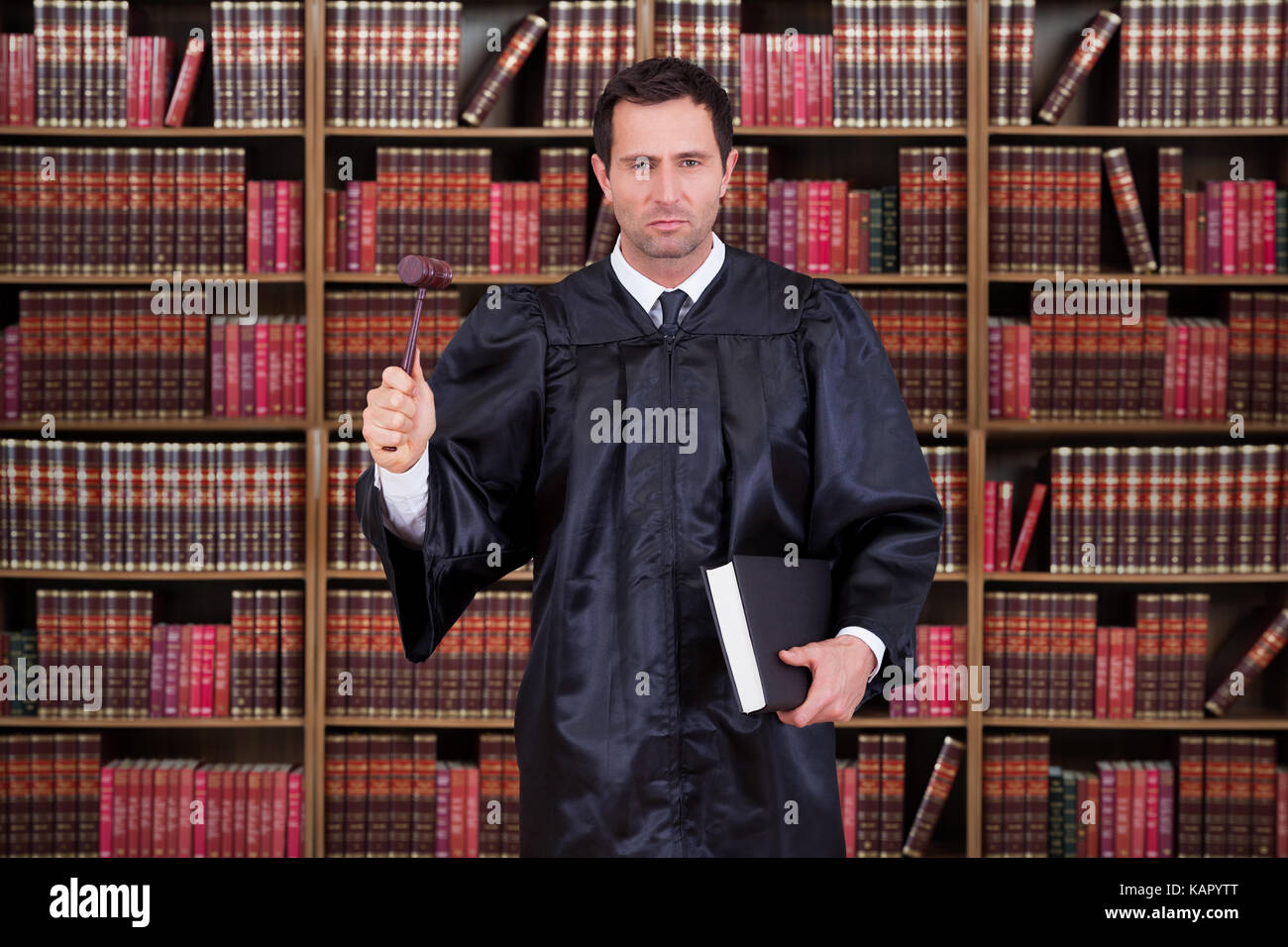 Portrait of serious judge holding gavel and book against shelves Stock ...