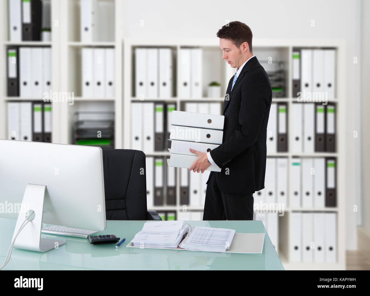 Side view of young businessman carrying binders by desk in office Stock ...