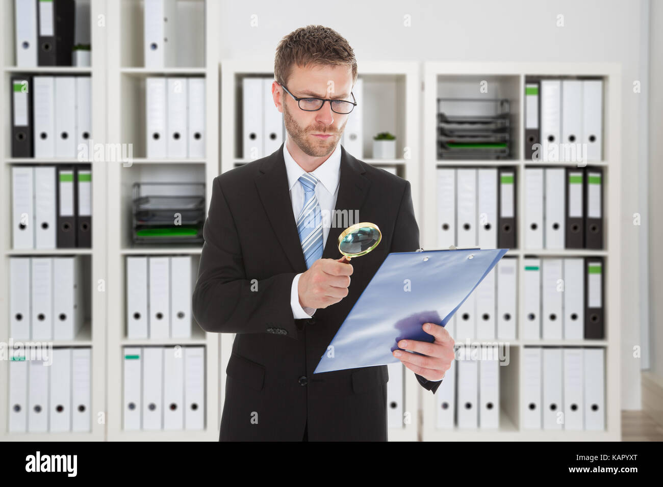Young businessman looking at document through magnifying glass in ...