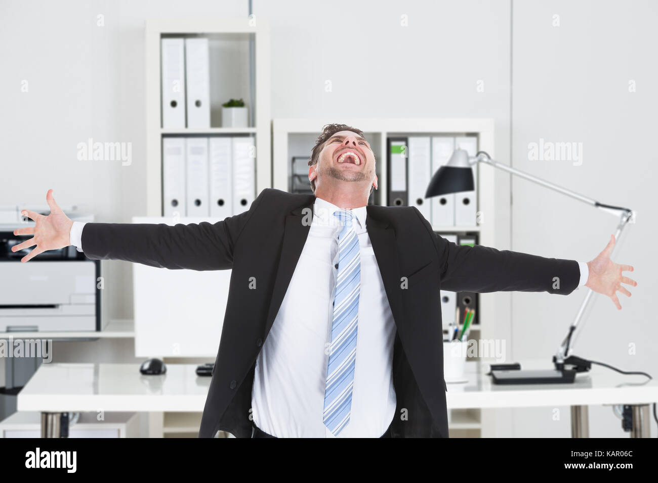 Happy young businessman laughing while standing with arms outstretched ...