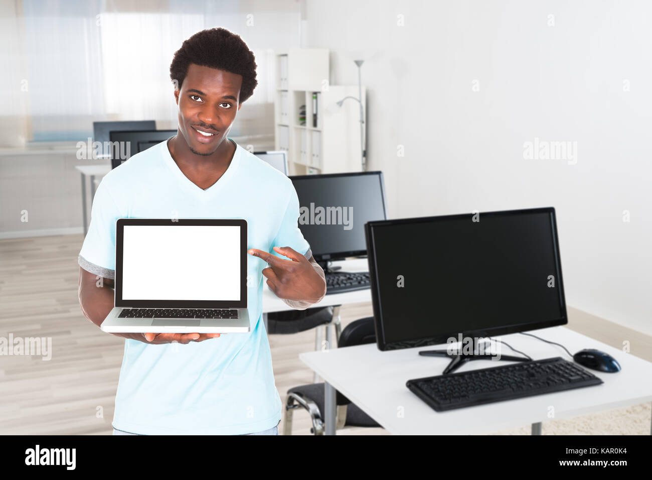 Portrait of confident young male nurse pointing at laptop in clinic ...