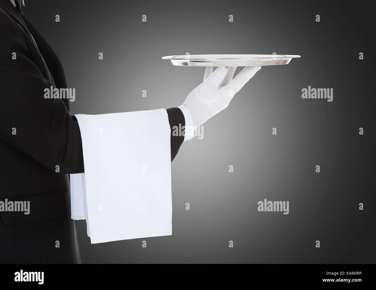Midsection of waiter with napkin holding empty silver tray over gray ...