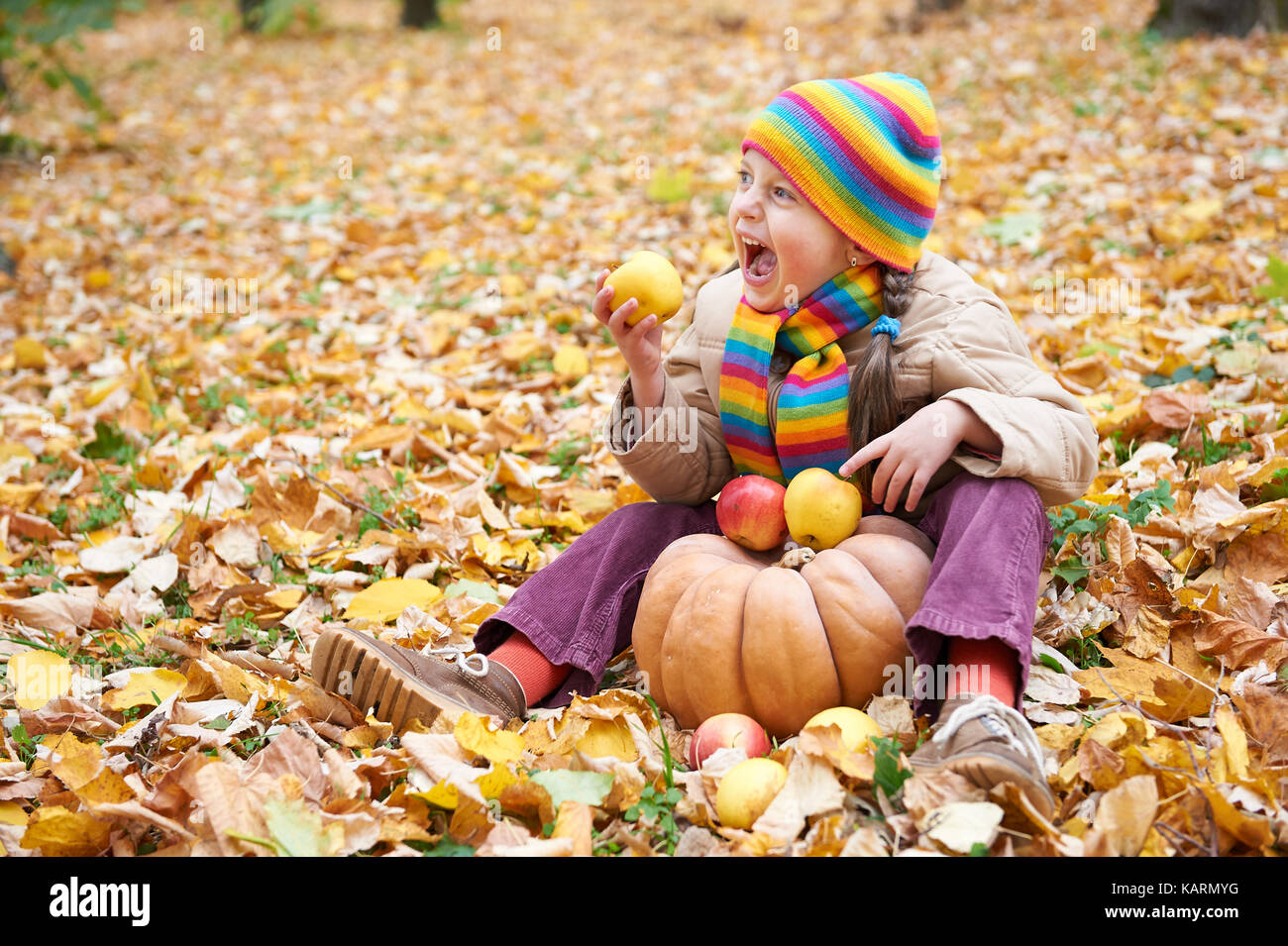 child eat apple and pumpkin in forest, sit on autumn leaves background ...