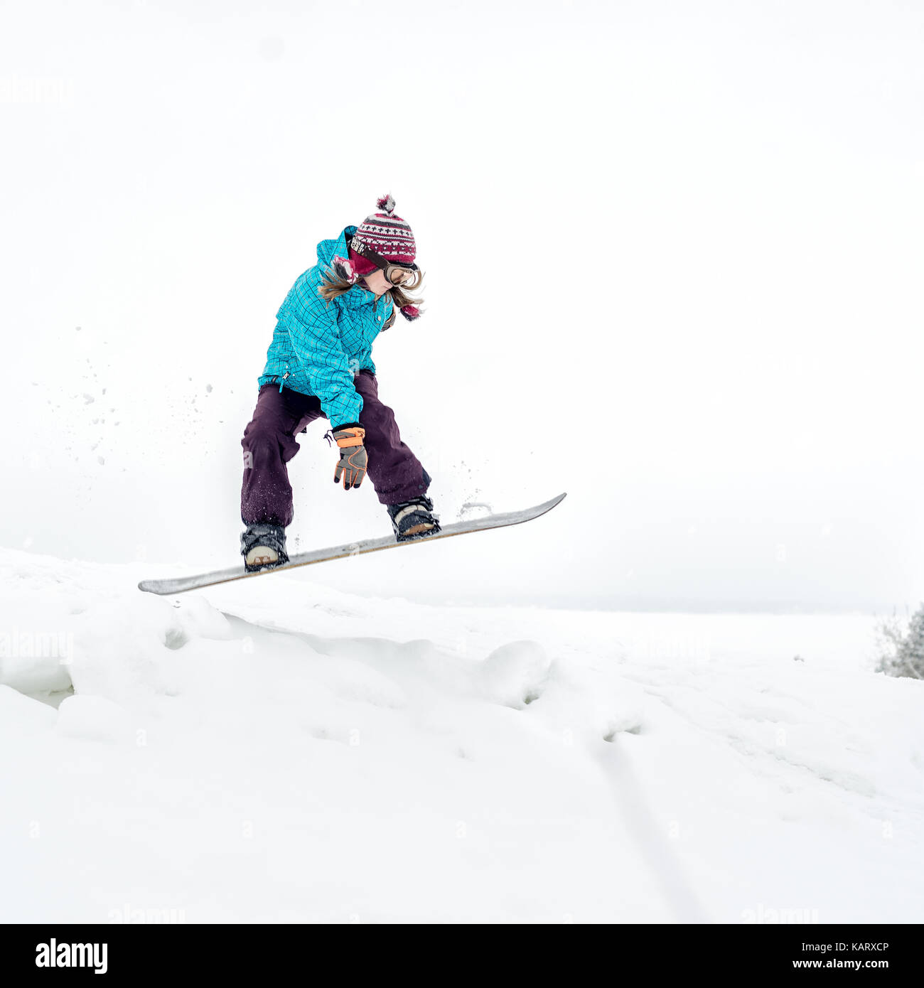 pretty young woman on the snowboard jumping over the slope in winter ...