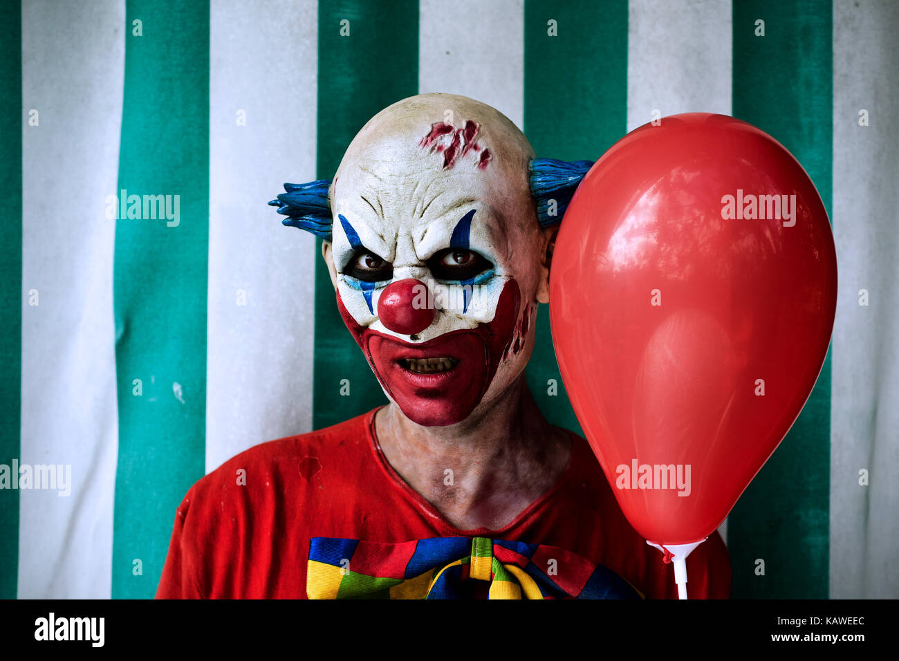 closeup of a scary evil clown wearing a dirty costume and holding a red ...