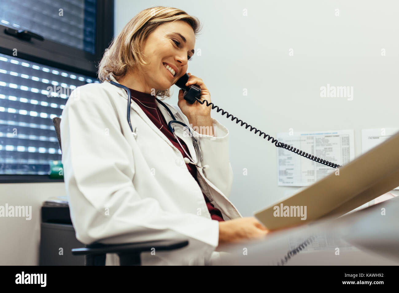 Female doctor reading medical reports and talking on phone at clinic ...
