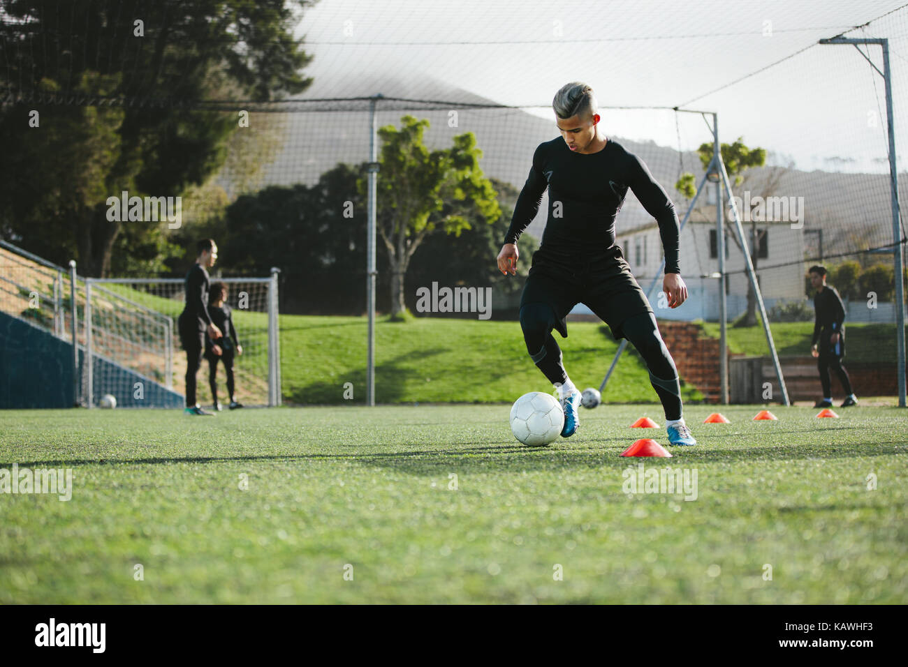Young soccer player training in football field with team in background ...