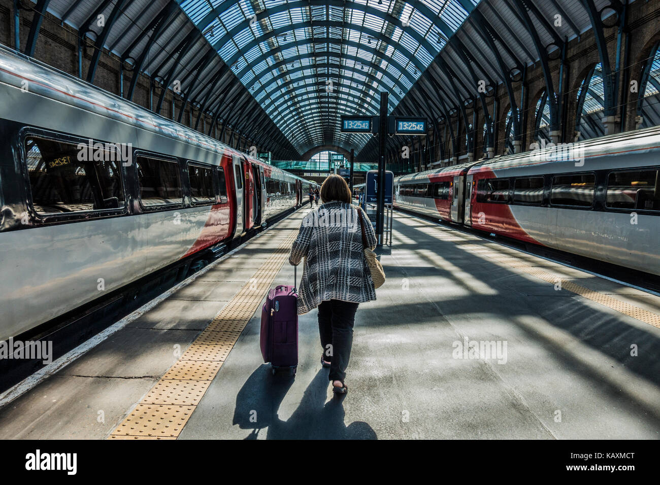 A woman pushing a suitcase along the platform, in strong sunlight ...